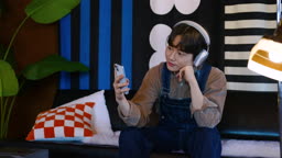 Gen Z - Man sitting on couch with headphones on and taking selfie ...